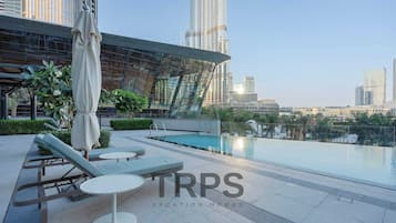 Uma área de piscina no terraço com espreguiçadeiras e um espaço de estar coberto, com vista para um horizonte urbano com edifícios altos.