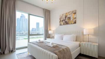 Quarto de hotel com uma cama grande, duas mesas de cabeceira, vista para a cidade e um lustre moderno.