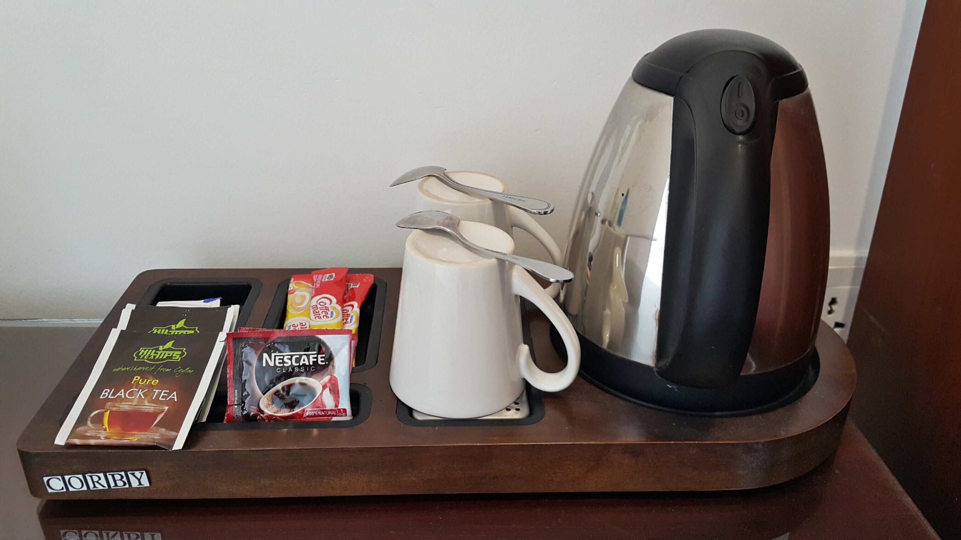 Uma bandeja com uma cafeteira, uma xícara branca, um sachê de café Nescafe Classic e um sachê de chá preto.