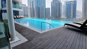 Piscina no terraço com espreguiçadeiras, rodeada por edifícios altos.