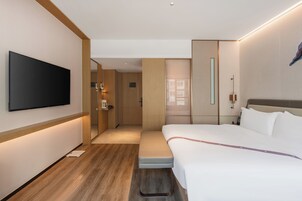 Quarto de hotel com uma cama grande, televisão de tela plana na parede, mesa de cabeceira e piso de madeira.