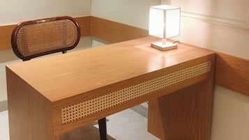 Escritório de canto com escrivaninha de madeira, uma cadeira, uma luminária e um painel decorativo na parede.