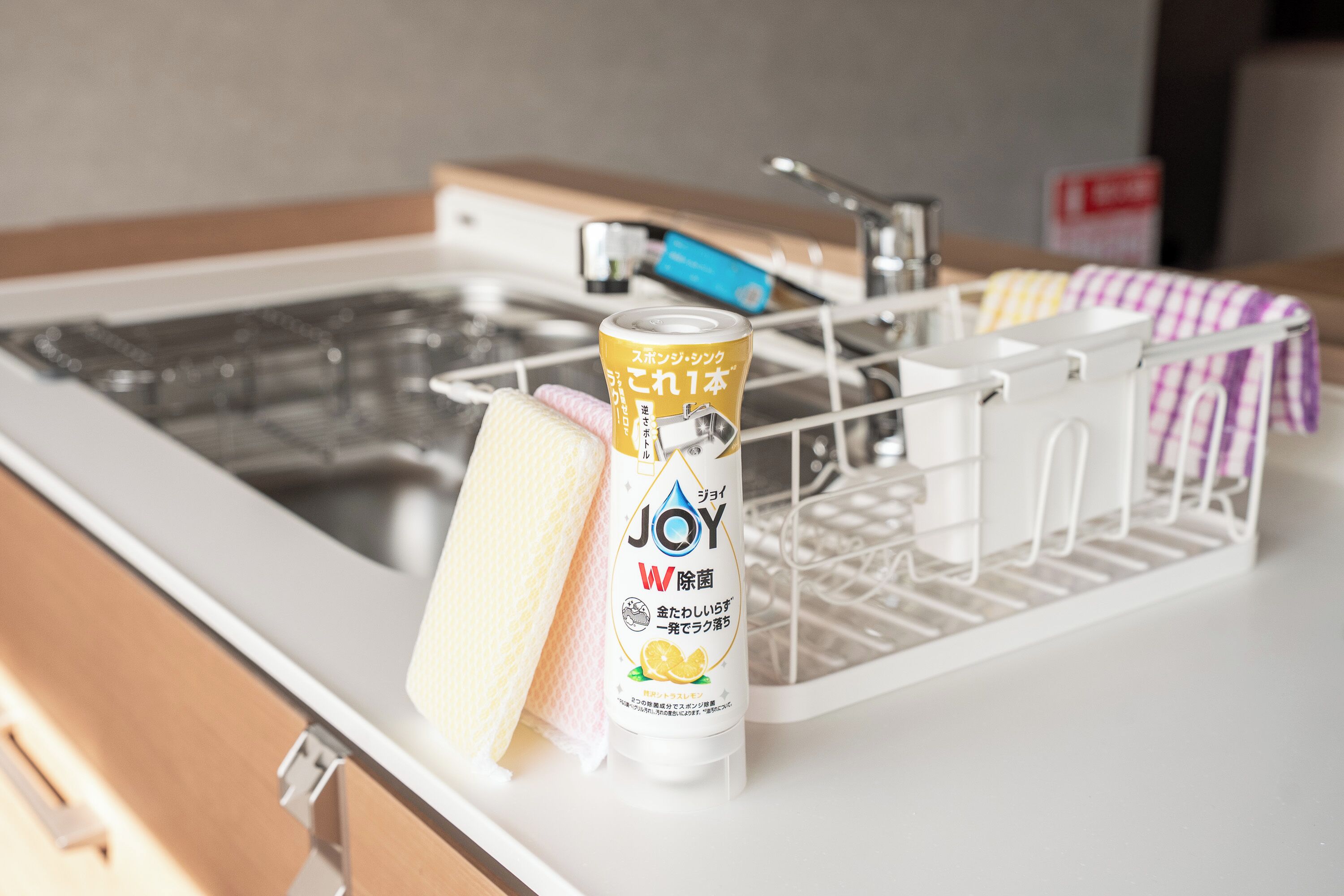 Uma pia de cozinha com um escorredor de louça contendo uma esponja e uma embalagem de detergente 'JOY'.