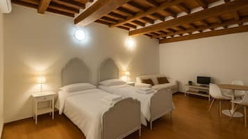 Quarto de hotel com duas camas, uma escrivaninha, uma cadeira e uma televisão.