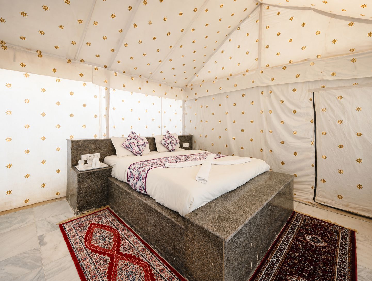 Quarto em estilo de tenda, com cama, mesas de cabeceira e tapetes estampados.
