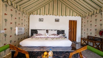 Quarto de hotel com cama, mesa com frutas e uma garrafa, e uma cadeira de madeira.