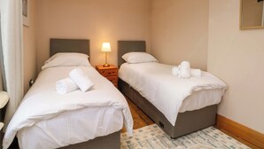 Quarto de hotel com duas camas de solteiro, uma mesa de cabeceira com abajur e um espelho na parede.
