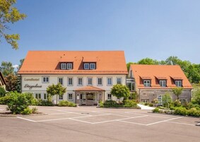 Um hotel de dois andares com telhado de telhas vermelhas, entrada central e estacionamento.