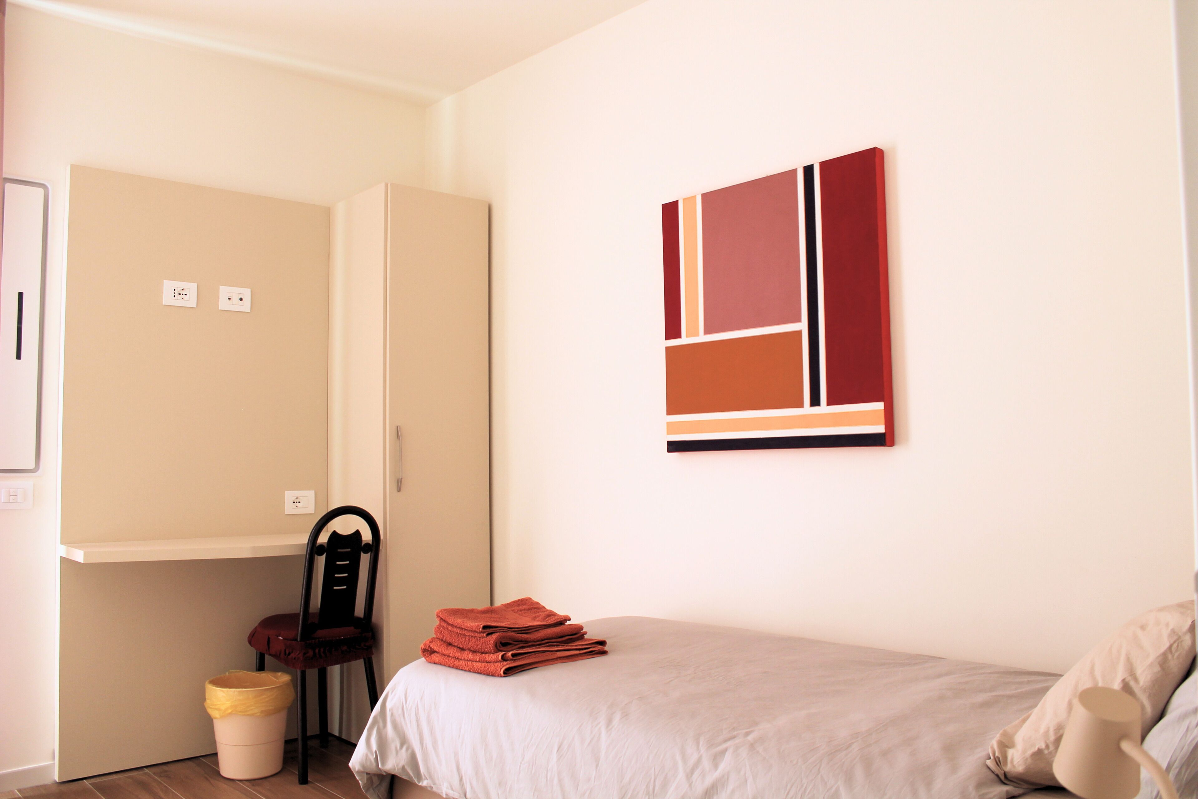 Quarto com cama, cadeira, obra de arte na parede e lixeira.