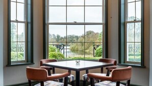 Uma sala de jantar com uma mesa redonda, seis cadeiras e uma janela grande com vista para áreas verdes e um corpo d'água.