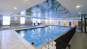 Piscina interna com água cristalina, deck ladrilhado e um mural no teto.