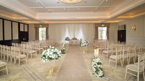 Um espaço para eventos formais, com fileiras de cadeiras, um corredor central e um candelabro.