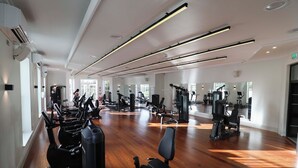 Uma academia com equipamentos de exercícios, piso de madeira e janelas amplas.