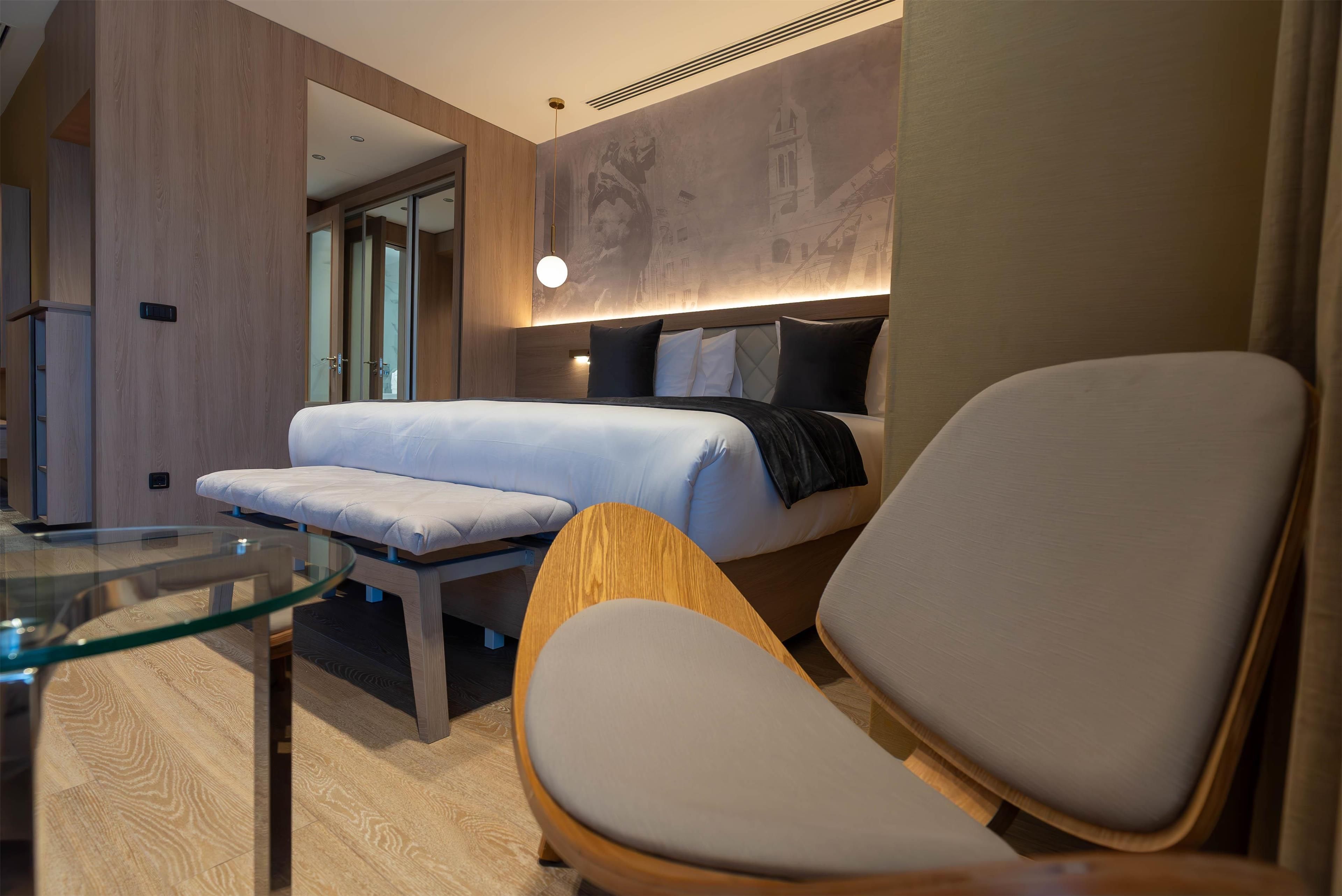 Quarto de hotel moderno com uma cama, um espaço de estar e uma mesa de vidro.