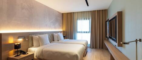 Quarto de hotel com duas camas, uma escrivaninha, uma televisão e uma mesa de cabeceira com abajur.