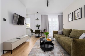 Uma sala de estar moderna com sofá, mesa de centro com um vaso e doces, TV fixada na parede e área de jantar com cadeiras e mesa.