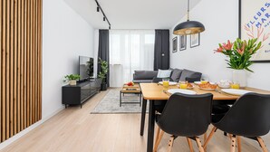 Uma sala de estar moderna com área de jantar, apresentando piso de madeira, um sofá, uma televisão e uma mesa de jantar com cadeiras.