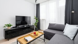 Uma sala de estar moderna com televisão de tela plana, um rack preto, um sofá cinza e uma mesa de centro de madeira com uma bandeja de frutas.
