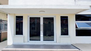 Entrada de um edifício moderno com porta e janelas de vidro, plataforma de concreto e grade de metal.