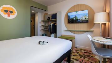 Quarto de hotel com uma cama, uma escrivaninha com cadeira, televisão e guarda-roupa.