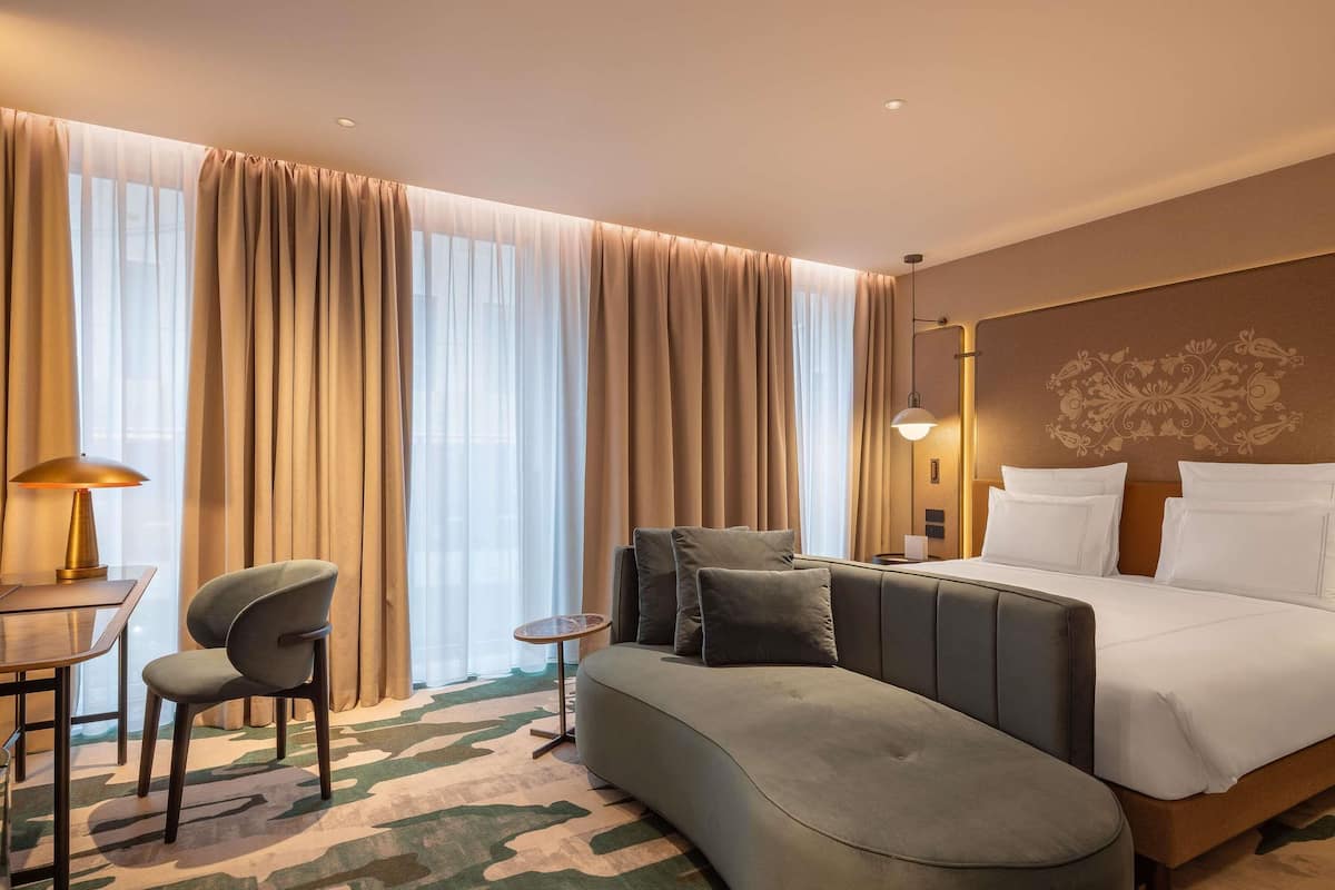 Quarto de hotel com cama, sofá, poltrona, mesinha e abajur.