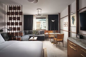 Quarto de hotel moderno com cama, sofá, mesa de jantar, cadeiras e televisão.
