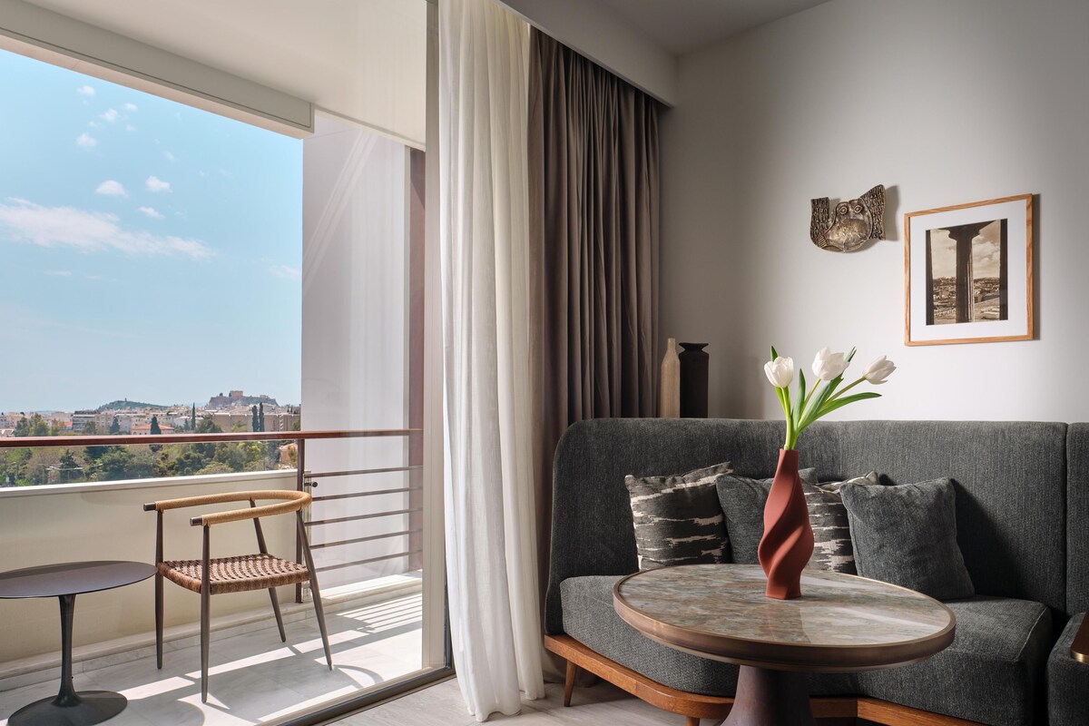 Uma varanda com vista para a paisagem urbana, um sofá com um vaso de flores e uma mesa pequena.