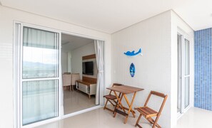 Quarto moderno com porta de vidro deslizante para uma varanda, uma pequena mesa de madeira com cadeiras e um painel decorativo azul na parede.