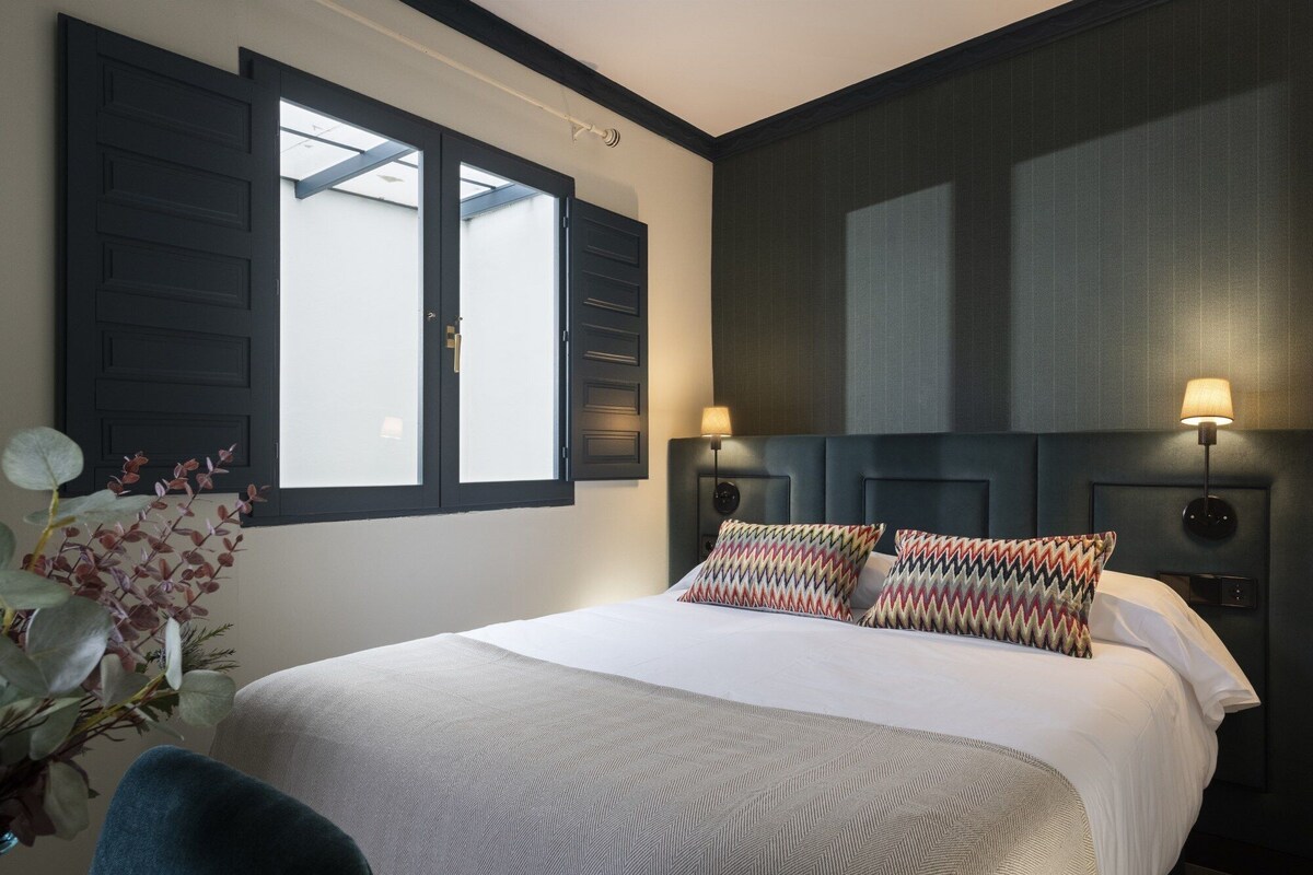 Um quarto com uma cama, duas luminárias de cabeceira, uma janela com persianas e uma planta.