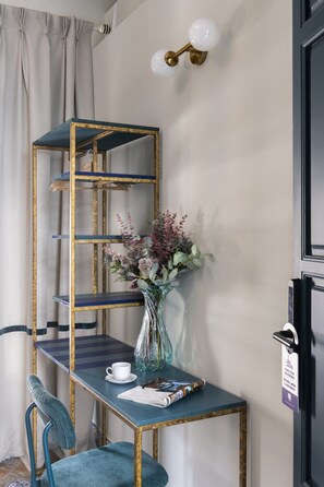 Quarto com cadeira azul, uma mesinha com um vaso de flores, estante e luminária na parede.