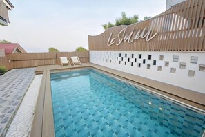 Piscina com padrão de azulejos, cerca de madeira e parede com placa de identificação.