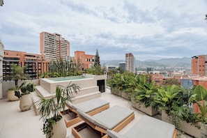 Terraço no telhado com espreguiçadeiras, piscina e plantas em vasos.