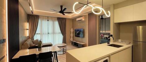 Uma cozinha moderna com máquina de lavar embutida, espaço de refeições com mesa e cadeiras, e sala de estar com sofá e televisão.