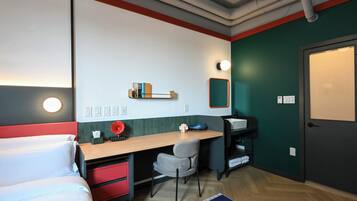 Quarto de hotel moderno com cama, escrivaninha, cadeira e pequena cozinha.