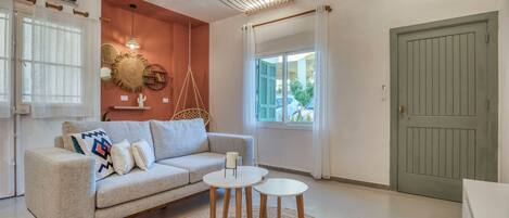 Uma sala de estar com sofá, duas mesinhas, luminária pendente e uma porta.