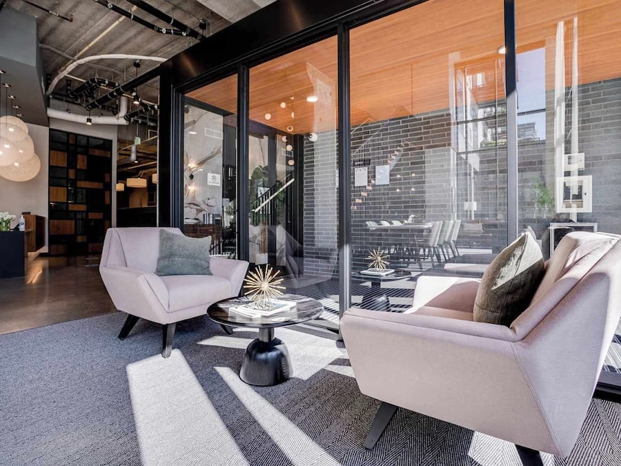 Um interior moderno com dois sofás, uma mesa de centro e uma parede de vidro que oferece vista para um edifício de tijolos.