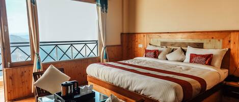 Quarto com estrutura de madeira, uma cama grande, uma mesinha com cafeteira e vista para as montanhas pela janela.