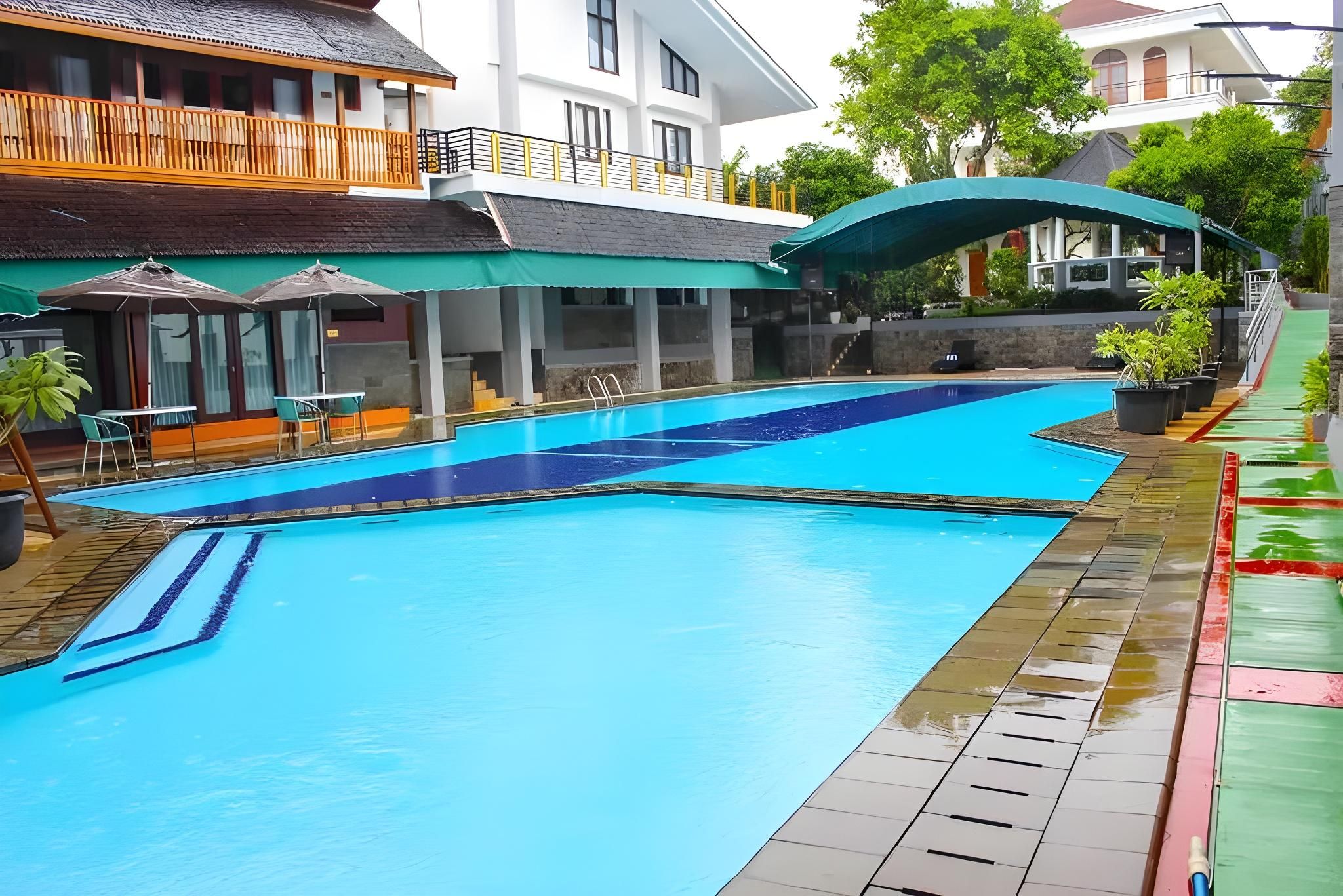 Piscina com superfície de água azul translúcida, rodeada por um deck de madeira e uma área de estar coberta com guarda-sóis.