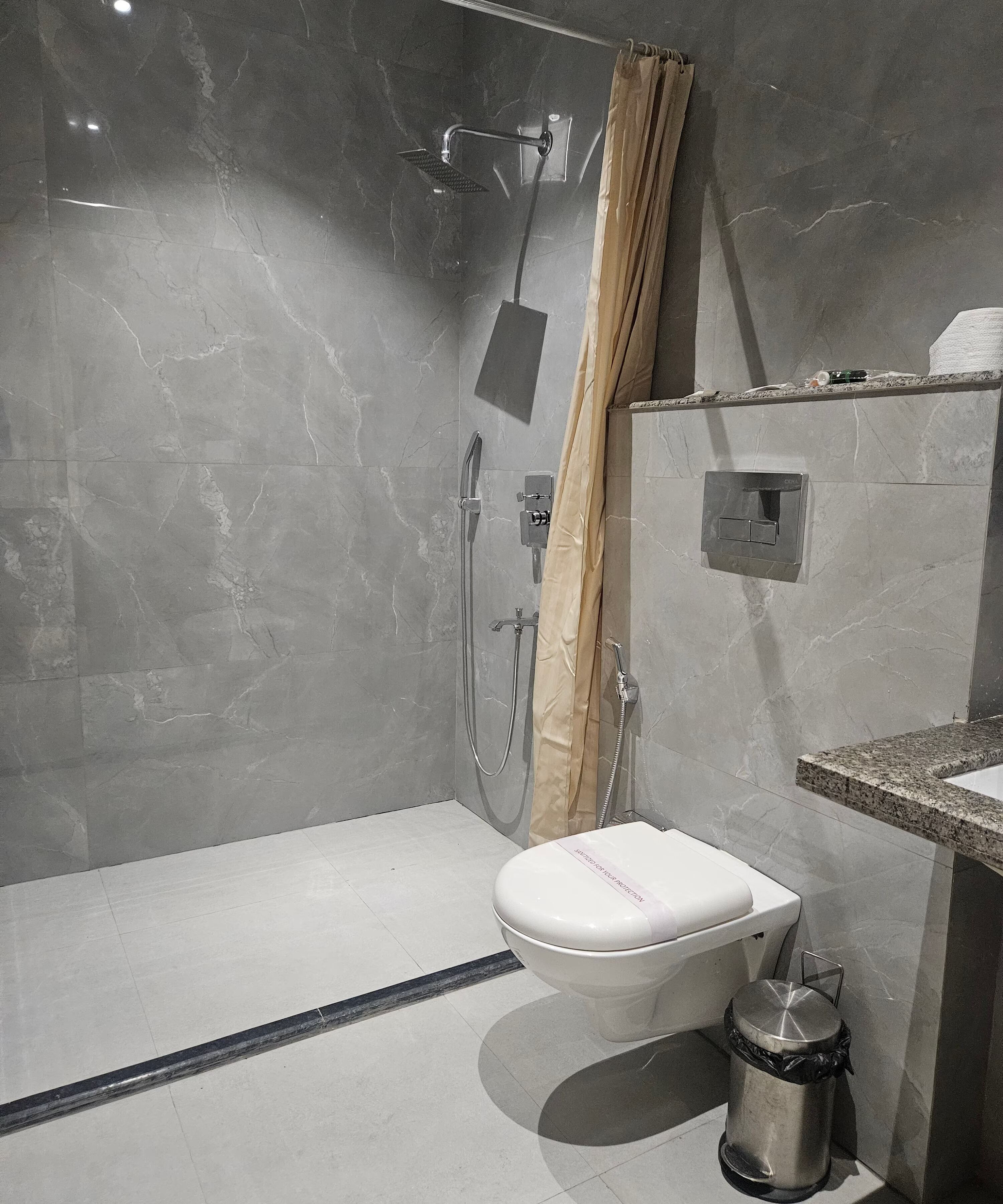 Casa de banho moderna com chuveiro, sanita e um cesto de lixo.
