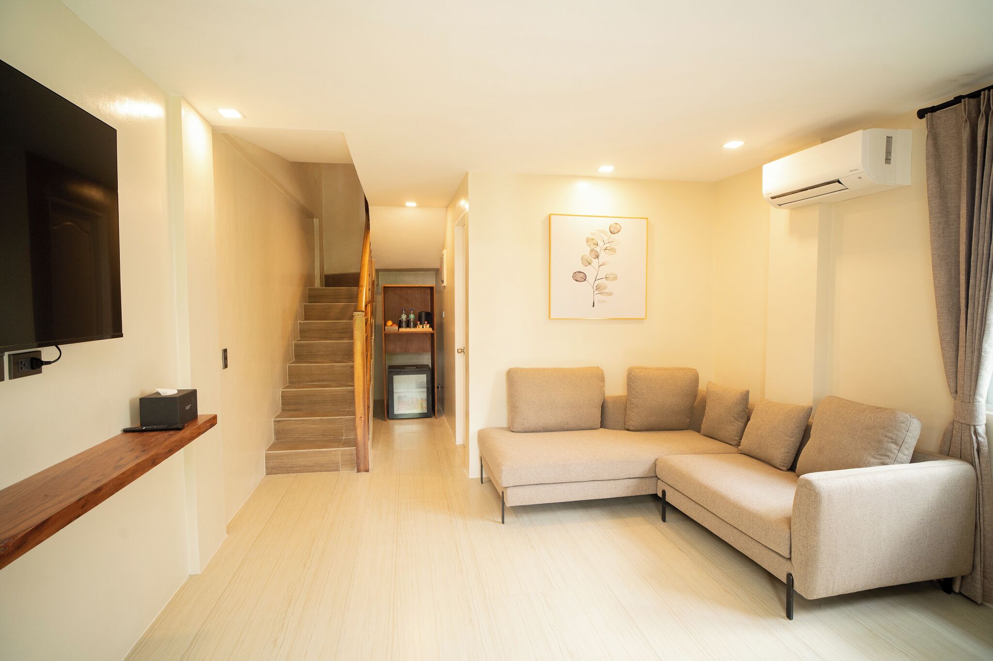 Uma sala de estar com sofá, TV de tela plana, escada e ar-condicionado.