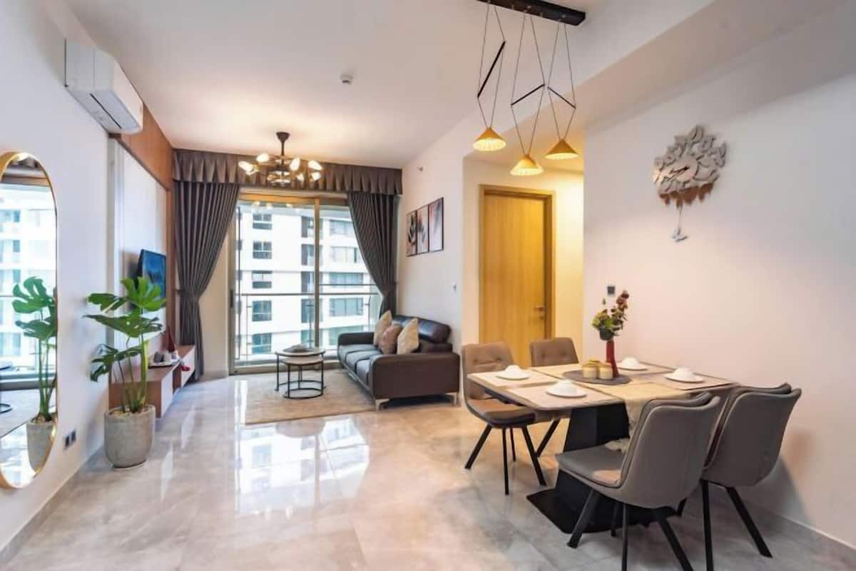 Uma sala de estar moderna com área de jantar, um sofá, uma mesa de centro e uma janela grande com cortinas.