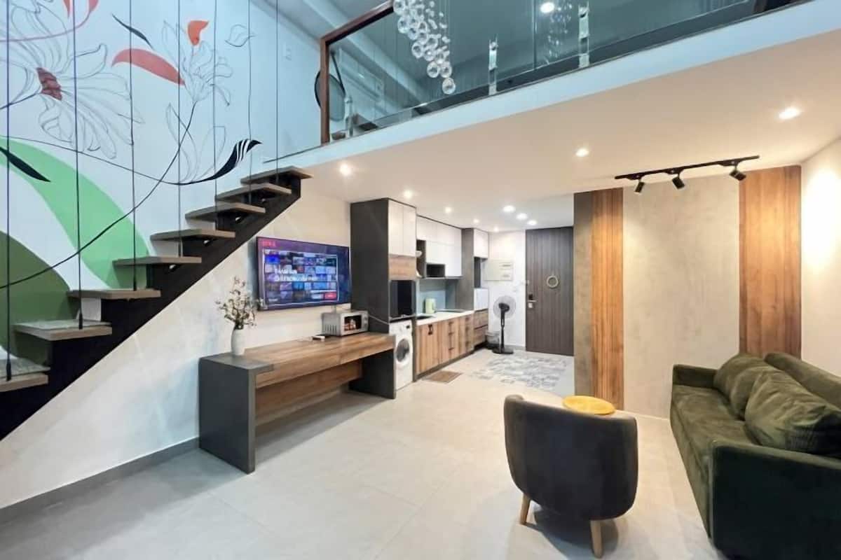 Um espaço de estar moderno com escada, televisão de tela plana, sofá e área de cozinha.