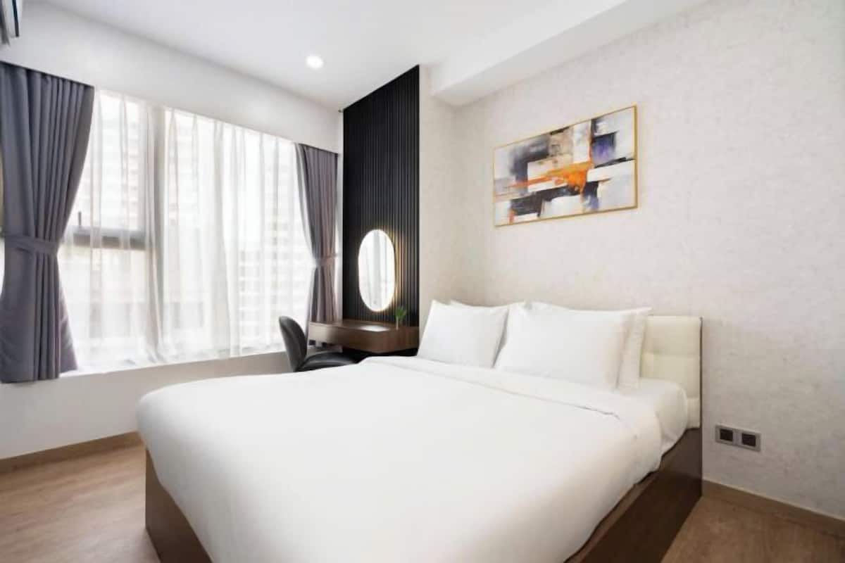 Quarto de hotel moderno com uma cama grande, uma escrivaninha com cadeira, um espelho redondo e um quadro na parede.