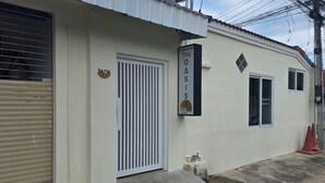 Um edifício com uma porta de obturador fechada, uma placa vertical com o texto "The Oasis" e uma pequena janela à direita.