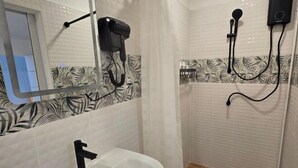 Casa de banho com lavatório branco, espelho, secador de cabelo e chuveiro com chuveiro manual.