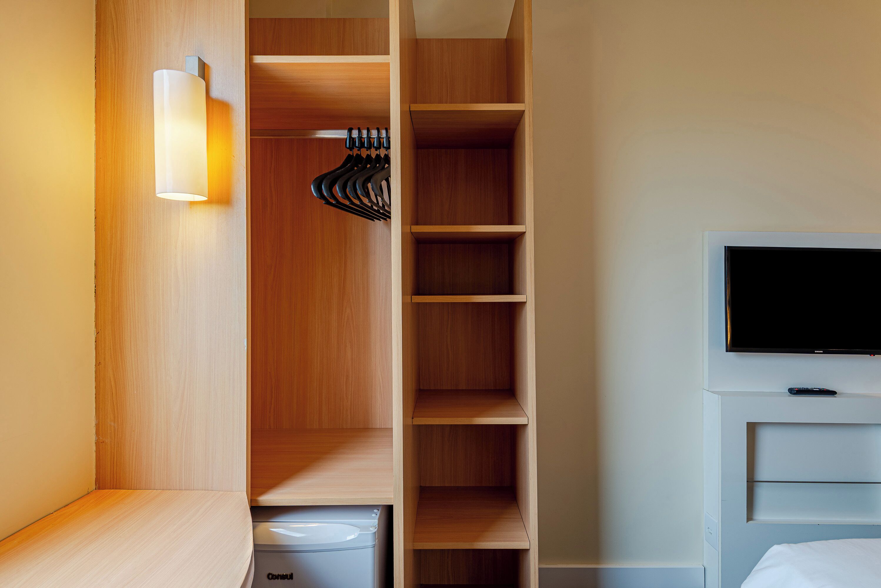 Quarto de hotel com guarda-roupa de madeira, televisão integrada e máquina de lavar roupa.