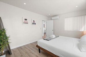 Quarto de hotel moderno com cama bem arrumada, planta em vaso e obra de arte na parede.