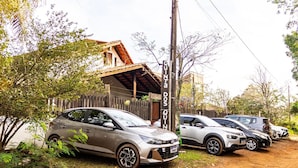 Fila de carros estacionados em área rural, com cerca de madeira e vegetação.