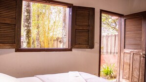 Um quarto com uma cama, uma janela com persianas de madeira e uma porta.