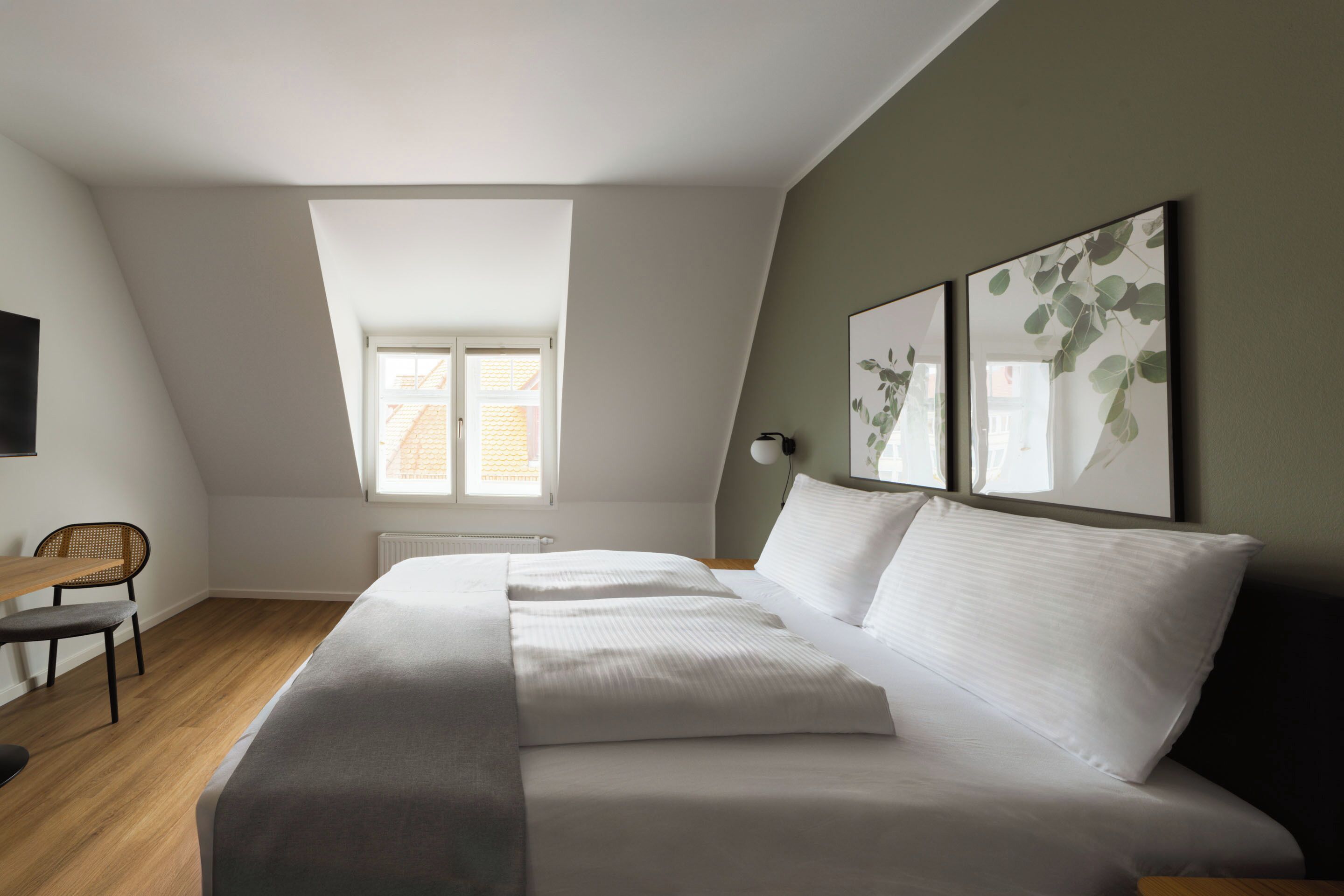 Quarto com cama, escrivaninha e cadeira. Há uma janela com persianas e um radiador.